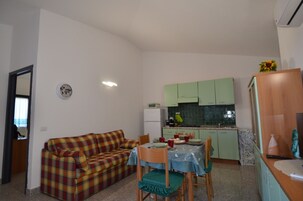 Um espaço compacto com sofá, mesa de jantar, cadeiras, cozinha compacta e um pequeno frigorífico.