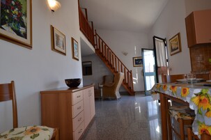 Uma área de refeições com escada de madeira, uma mesa com toalha florida e uma cozinha com fogão.