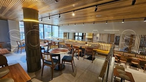 Restaurante moderno com teto de madeira, mesas redondas e áreas de estar com assentos acolchoados.