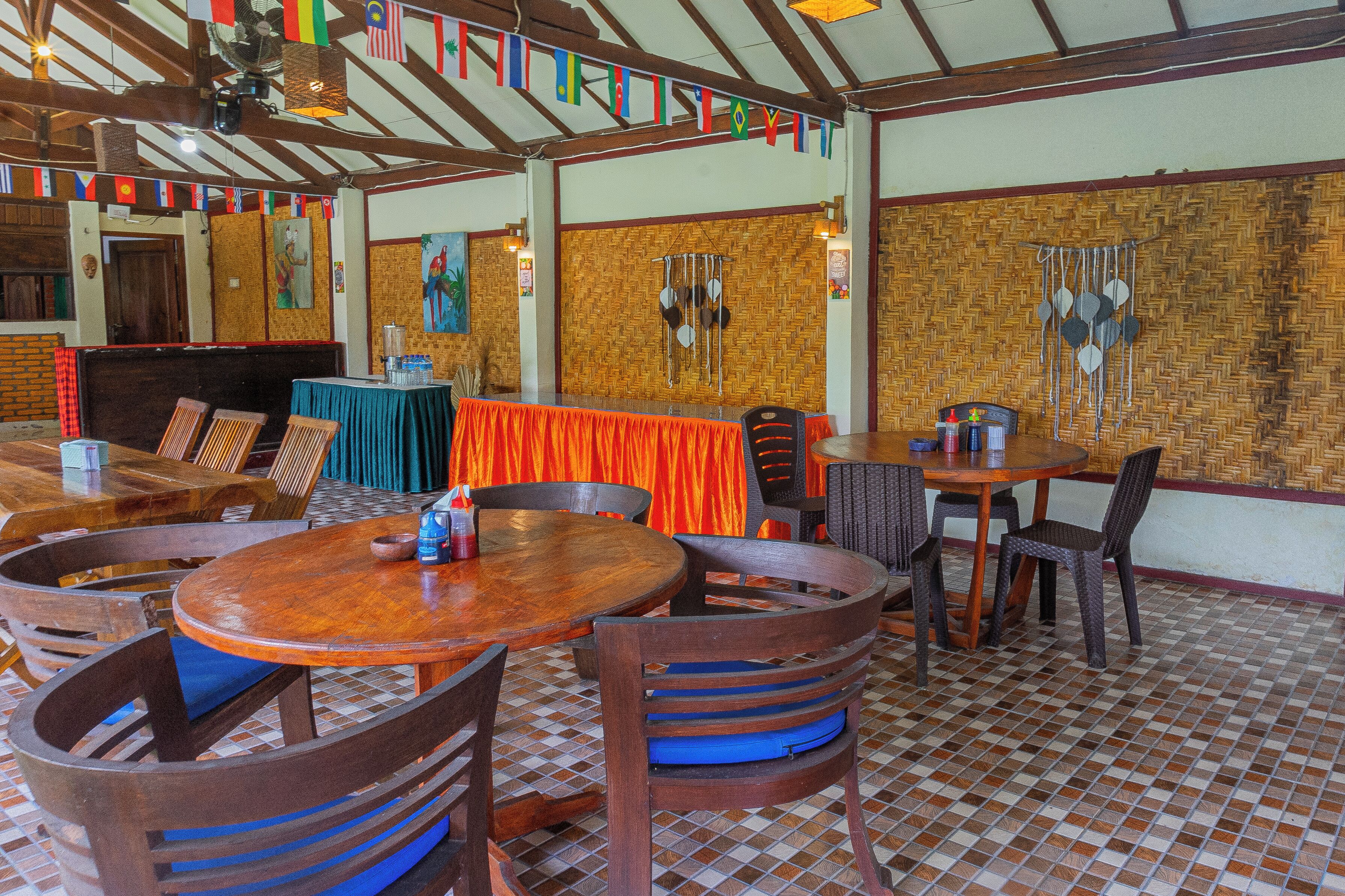 Um restaurante com mesas e cadeiras de madeira, piso de azulejos e parede com padrão trançado.