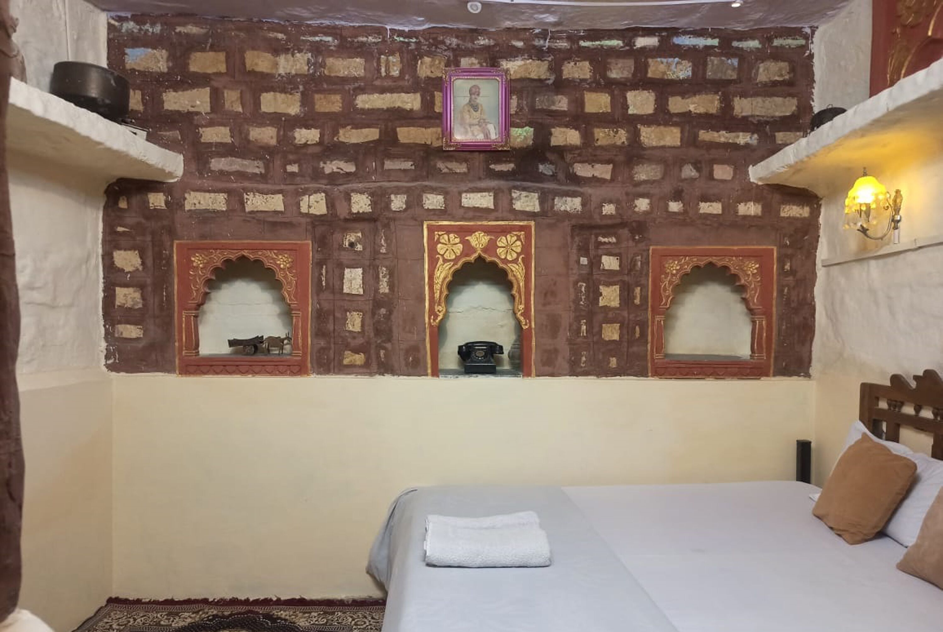 Quarto com uma cama, uma pequena estante com uma panela e arcos decorativos na parede.
