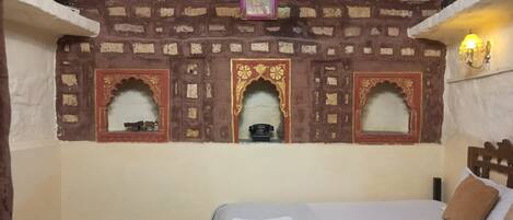 Quarto com uma cama, uma pequena estante com uma panela e arcos decorativos na parede.