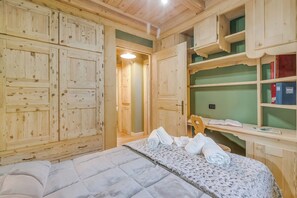 Um quarto de madeira com uma cama, uma escrivaninha e um guarda-roupa.