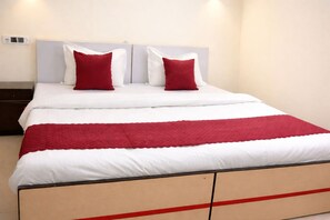 Cama com roupa de cama branca e vermelha, cabeceira de madeira e faixa decorativa vermelha.