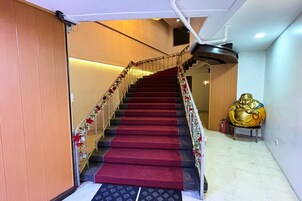 Uma escadaria com degraus revestidos de carpete vermelho e detalhes florais, que dá acesso a um andar superior.
