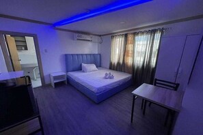 Quarto de hotel com uma cama de solteiro, mesa de cabeceira, escrivaninha e guarda-roupa.