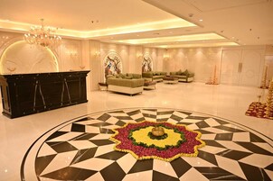 Um hall espaçoso com piso estampado em padrão geométrico, um arranjo floral central, um lustre imponente e uma área de estar com sofás.