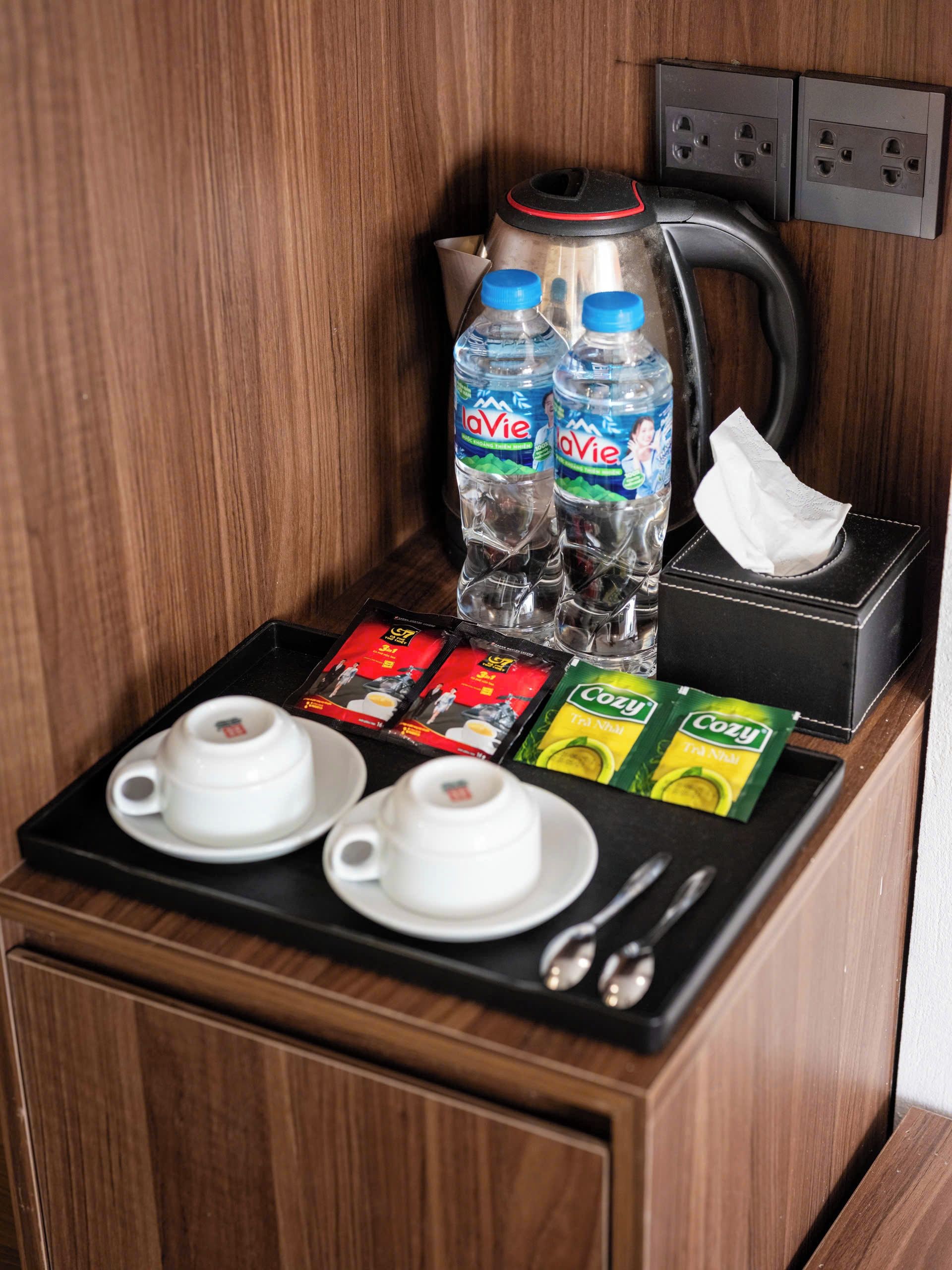 Minibar de hotel com água engarrafada, cafeteira e sachês de chá.