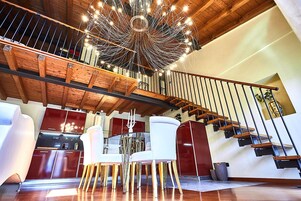 Uma sala de estar ampla com escada de madeira, móveis modernos e um lustre singular.