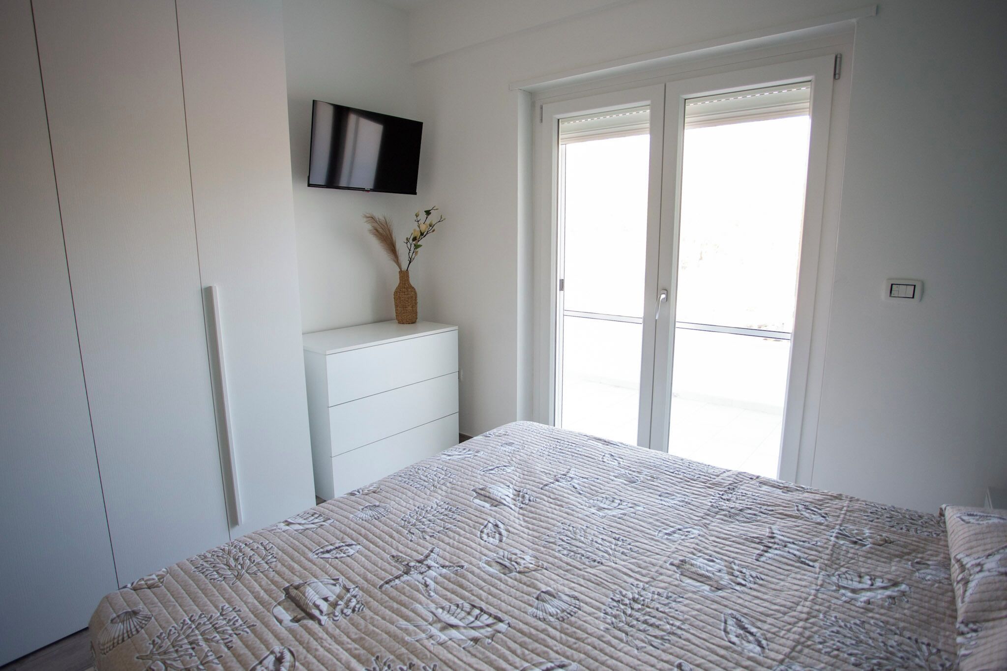Quarto com cama, cômoda, televisão e porta de vidro deslizante para o exterior.