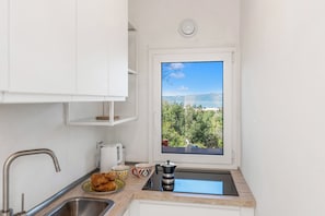 Uma cozinha com vista para uma paisagem montanhosa pela janela, pia, cafeteira e um prato de croissants.
