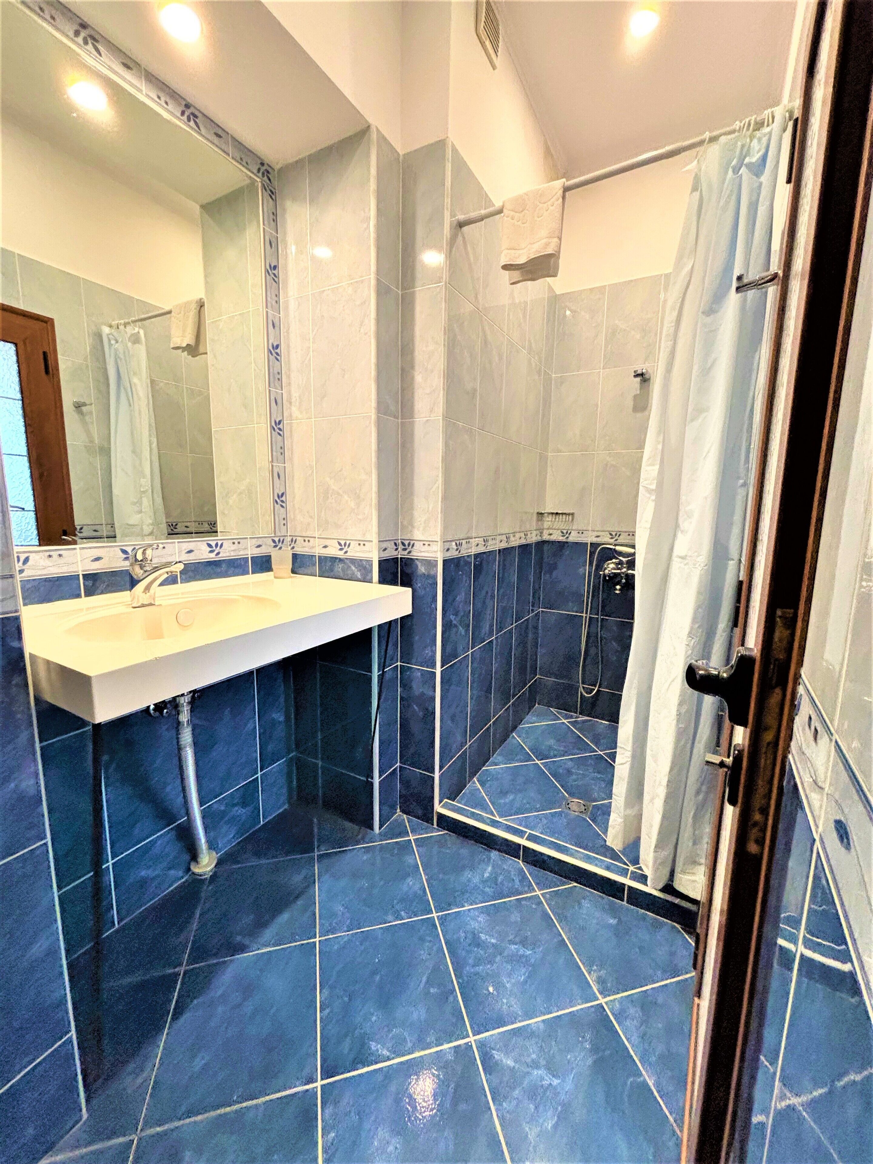 Uma casa de banho com uma pia branca, azulejos azuis e zona de duche.