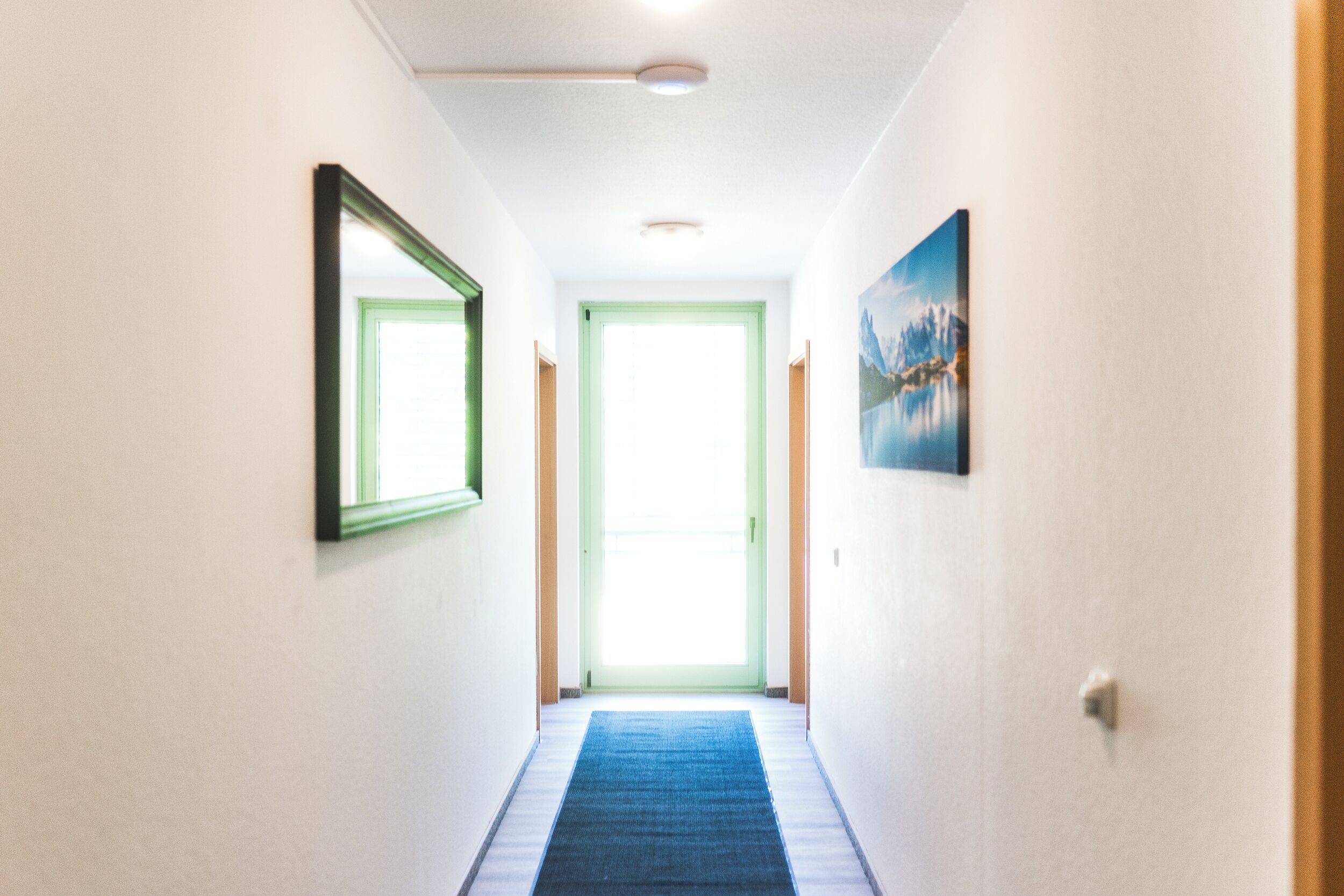 Um corredor com carpete azul, porta verde e um quadro pendurado na parede.
