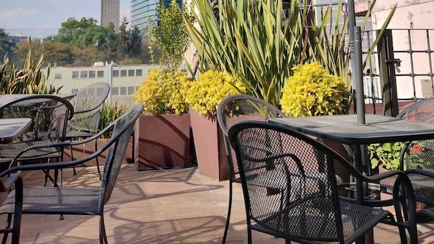 Um terraço no telhado com área de estar ao ar livre, cercado por edifícios altos e vegetação.