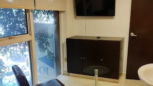 Quarto de hotel com cama, mesa pequena, televisão, armário e janela.