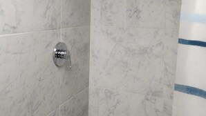 Casa de banho com azulejos de mármore, um chuveiro e um porta-toalhas.