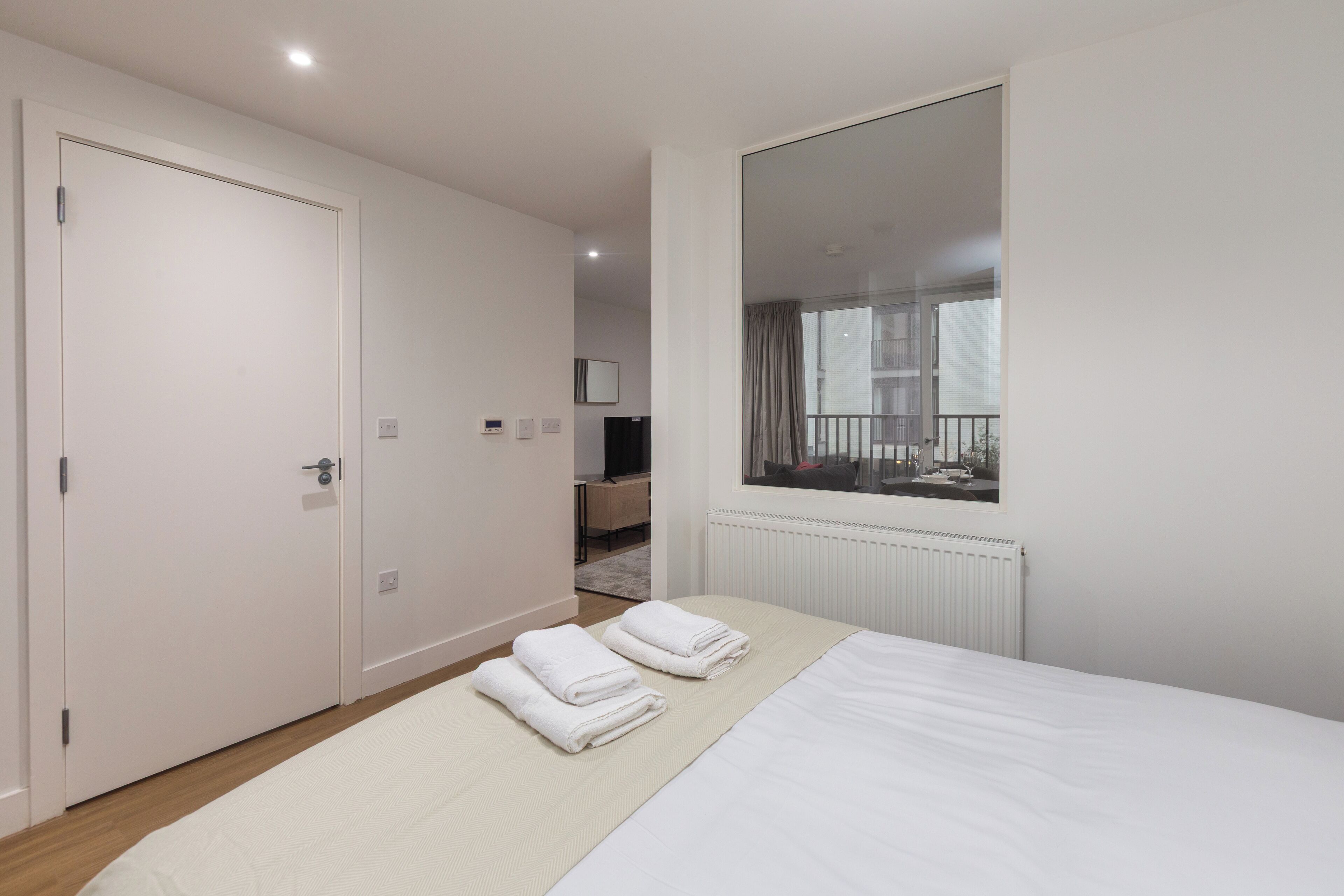 Quarto de hotel com uma cama grande, uma janela com vista para o exterior, uma porta e um espelho na parede.