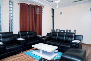 Uma sala de estar moderna com sofás de couro preto, uma mesa de centro branca e um tapete azul estampado.