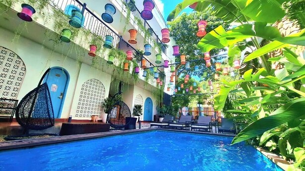 Uma área de piscina com piscina azul, cadeiras suspensas e uma varanda com decorações coloridas.