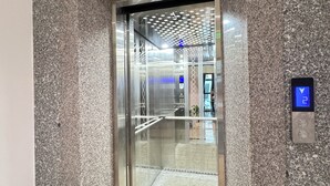 Um elevador com visor digital, paredes metálicas e um extintor próximo à base.