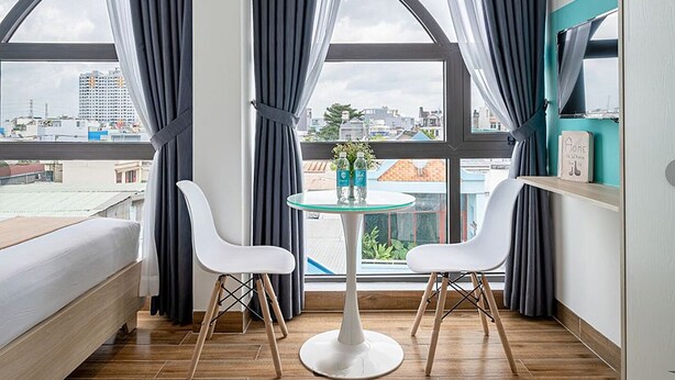 Quarto moderno com uma janela grande, duas cadeiras brancas, uma mesa de vidro e uma prateleira azul-esverdeada com uma moldura.