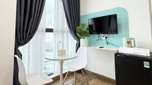 Quarto moderno com mesa de vidro, duas cadeiras brancas, frigorífico preto, televisão montada e um vaso com planta.