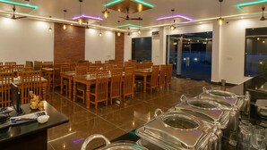Restaurante com mobiliário de madeira, ventiladores de teto e área de buffet com recipientes de vidro transparente.