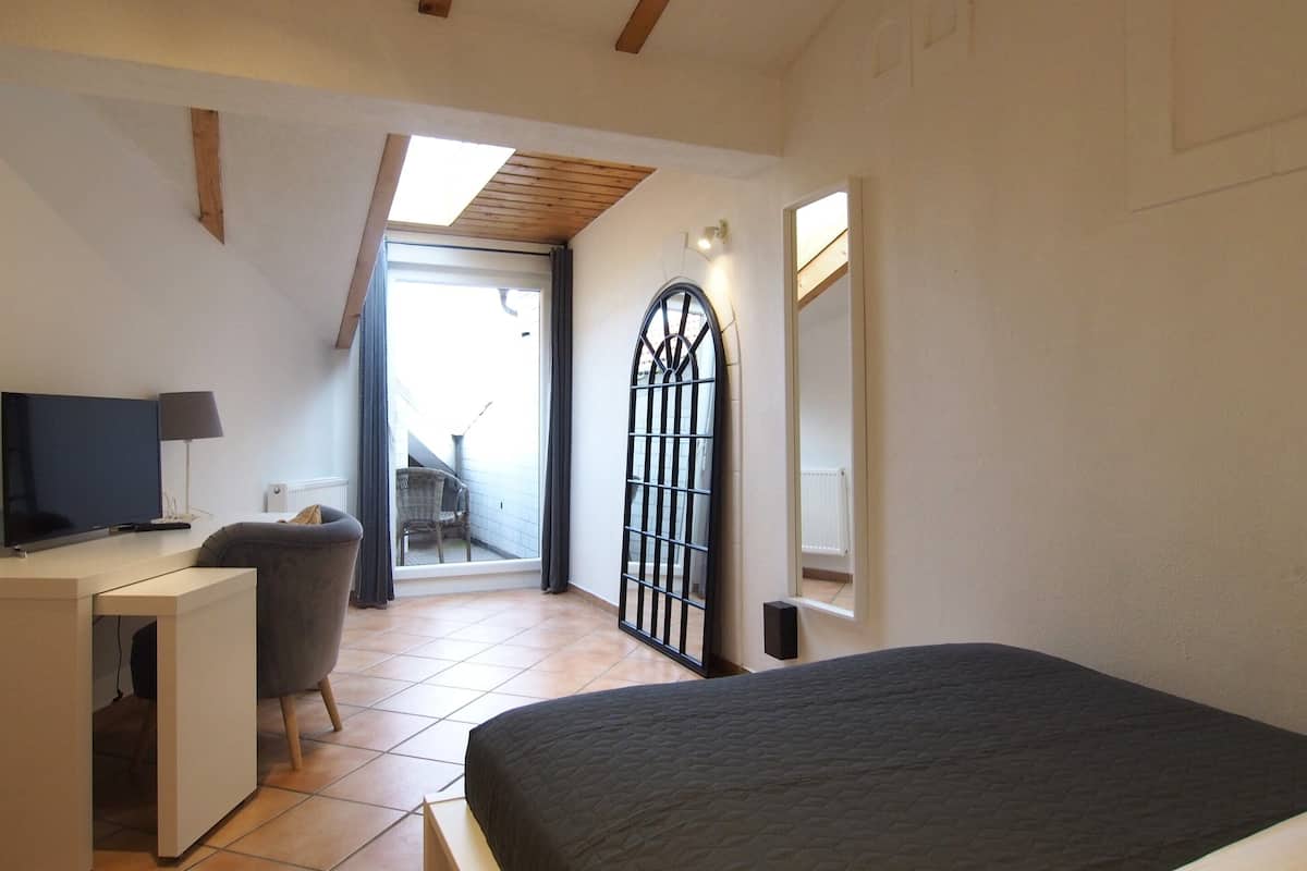 Quarto com cama, escrivaninha com televisão, cadeira e janela.