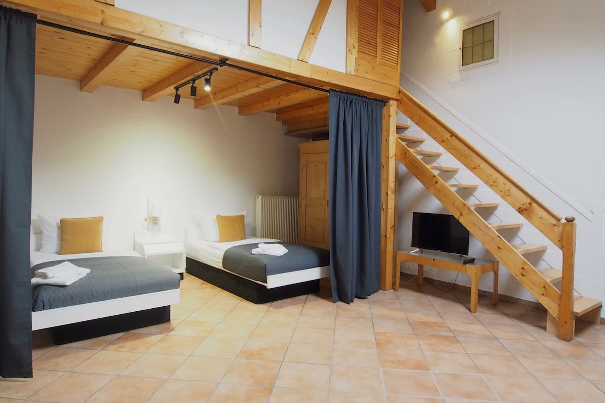Quarto com duas camas, escada de madeira e televisão sobre suporte de madeira.