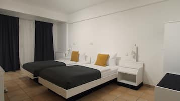 Quarto de hotel com duas camas de solteiro, mesas de cabeceira brancas, uma pequena mesa e uma janela com cortinas preto e branco.