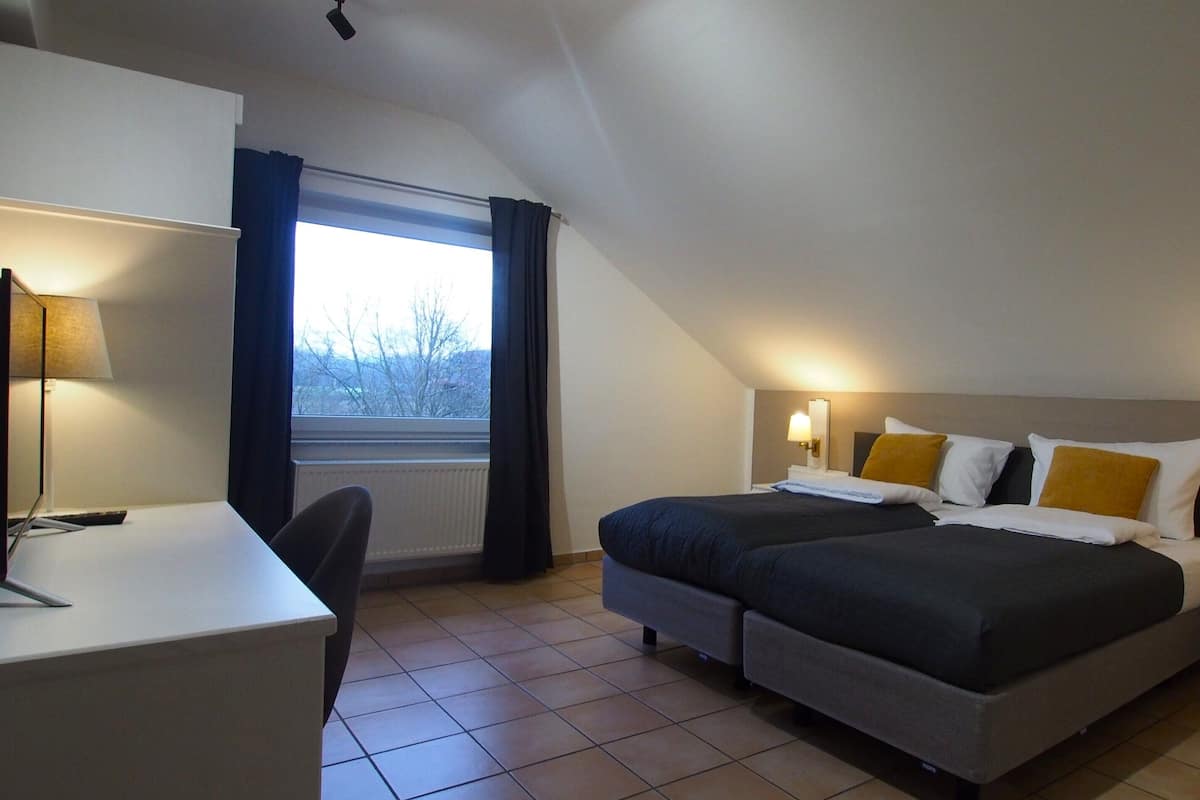 Quarto de hotel com uma cama, duas mesas de cabeceira, uma escrivaninha e uma cadeira.