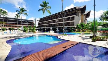 Um hotel com piscina, palmeiras e um edifício de vários andares.