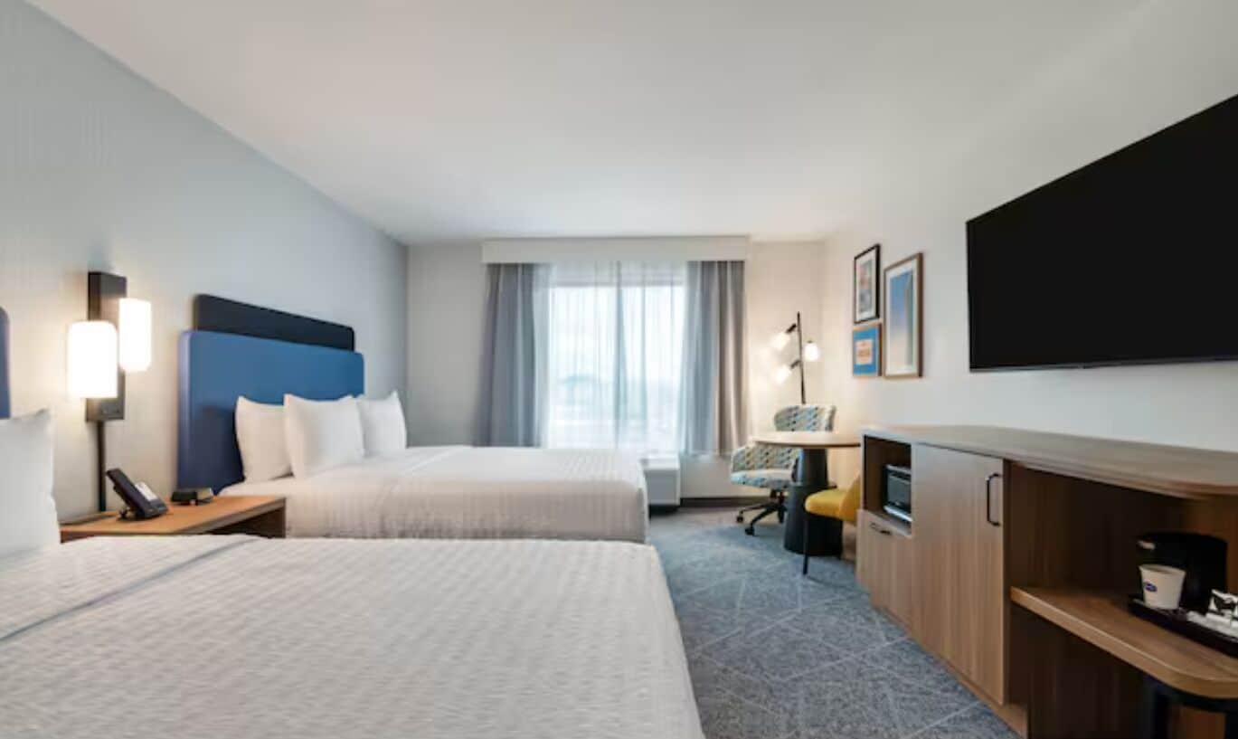 Quarto de hotel com duas camas, uma escrivaninha, televisão de tela plana e uma janela com cortinas.