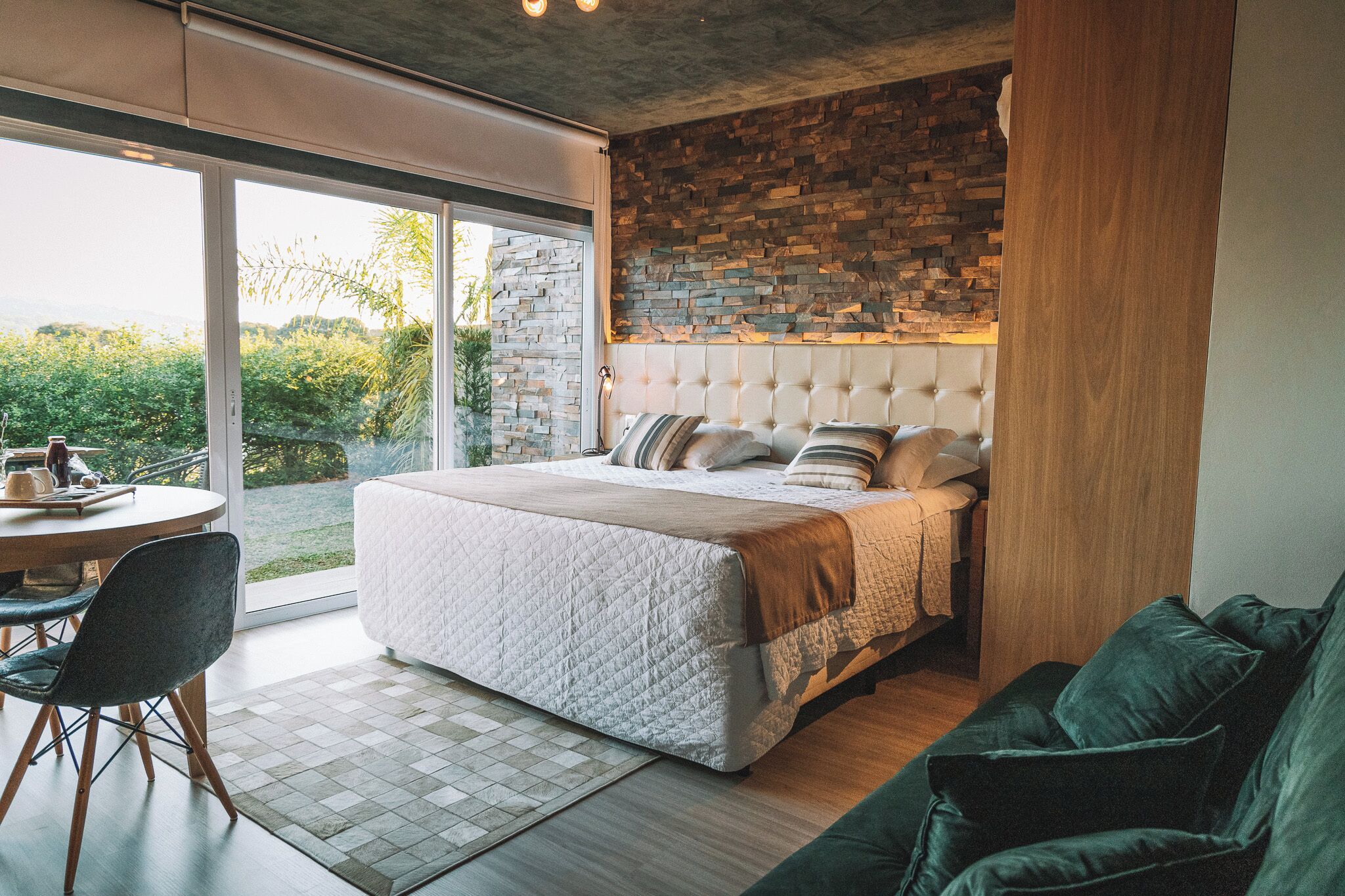 Quarto moderno com cama grande, cabeceira de madeira e vista para o verde lá fora.