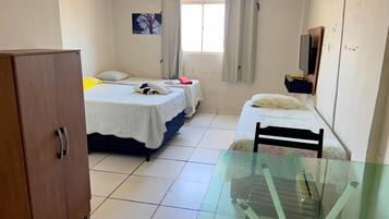 Quarto pequeno e bem iluminado, com duas camas, uma mesa de vidro e um guarda-roupa.