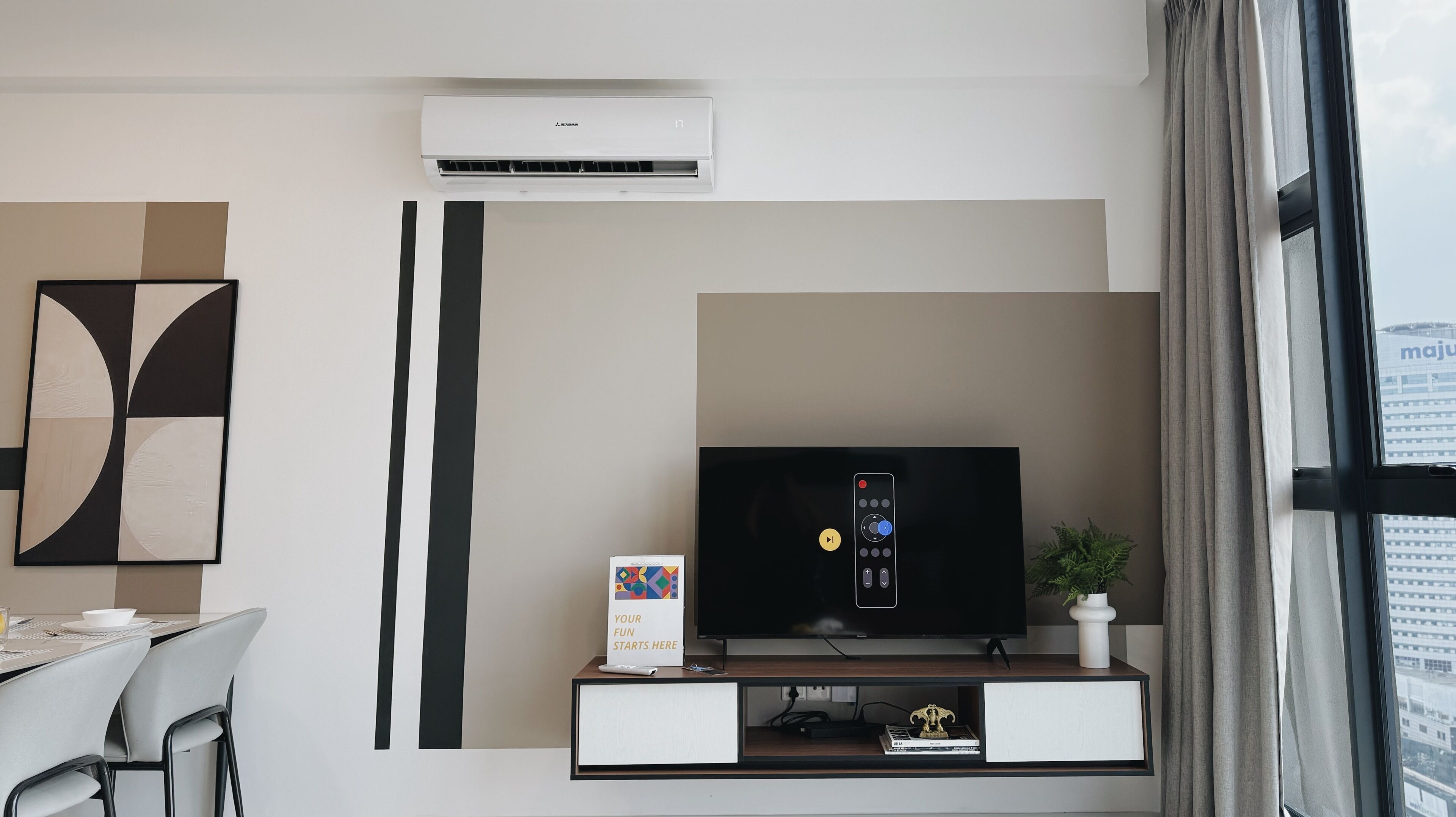 Uma sala de estar moderna com televisão de tela plana, um espaço de jantar com mesa e cadeiras, e uma janela grande com cortinas.