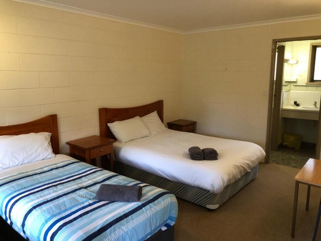 Quarto com duas camas, cabeceira de madeira, mesa de cabeceira e uma pequena mesa.