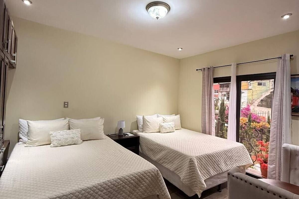 Quarto de hotel com duas camas, uma mesinha e uma cadeira.