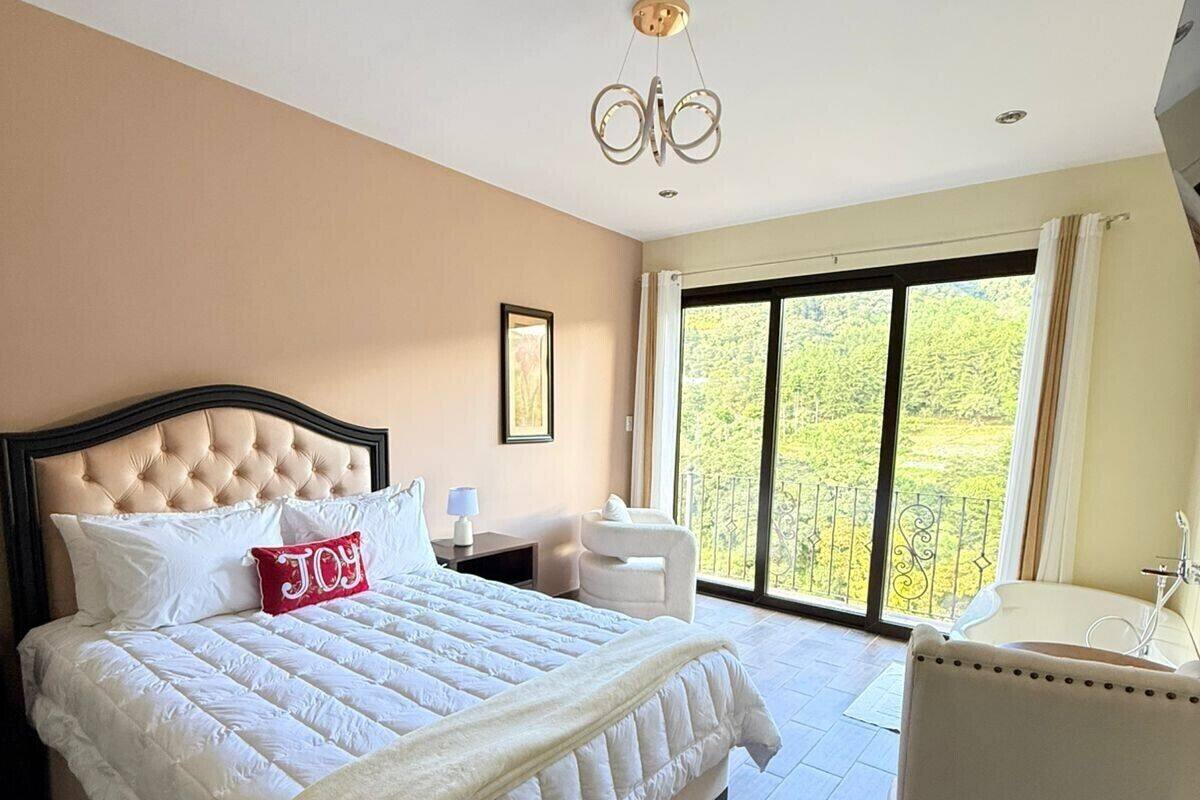 Quarto com cama grande, mesa de cabeceira, cadeira, janela com vista e luminária no teto.