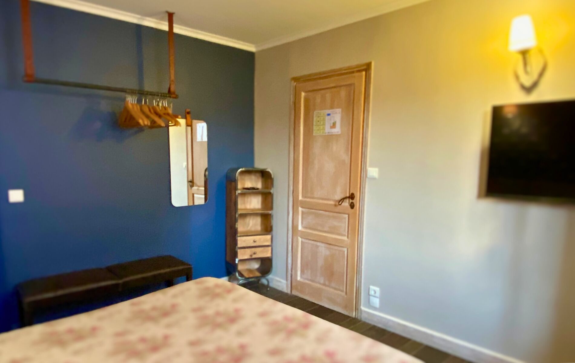 Quarto de hotel com cama, porta de madeira, luminária fixada na parede e televisão montada na parede.