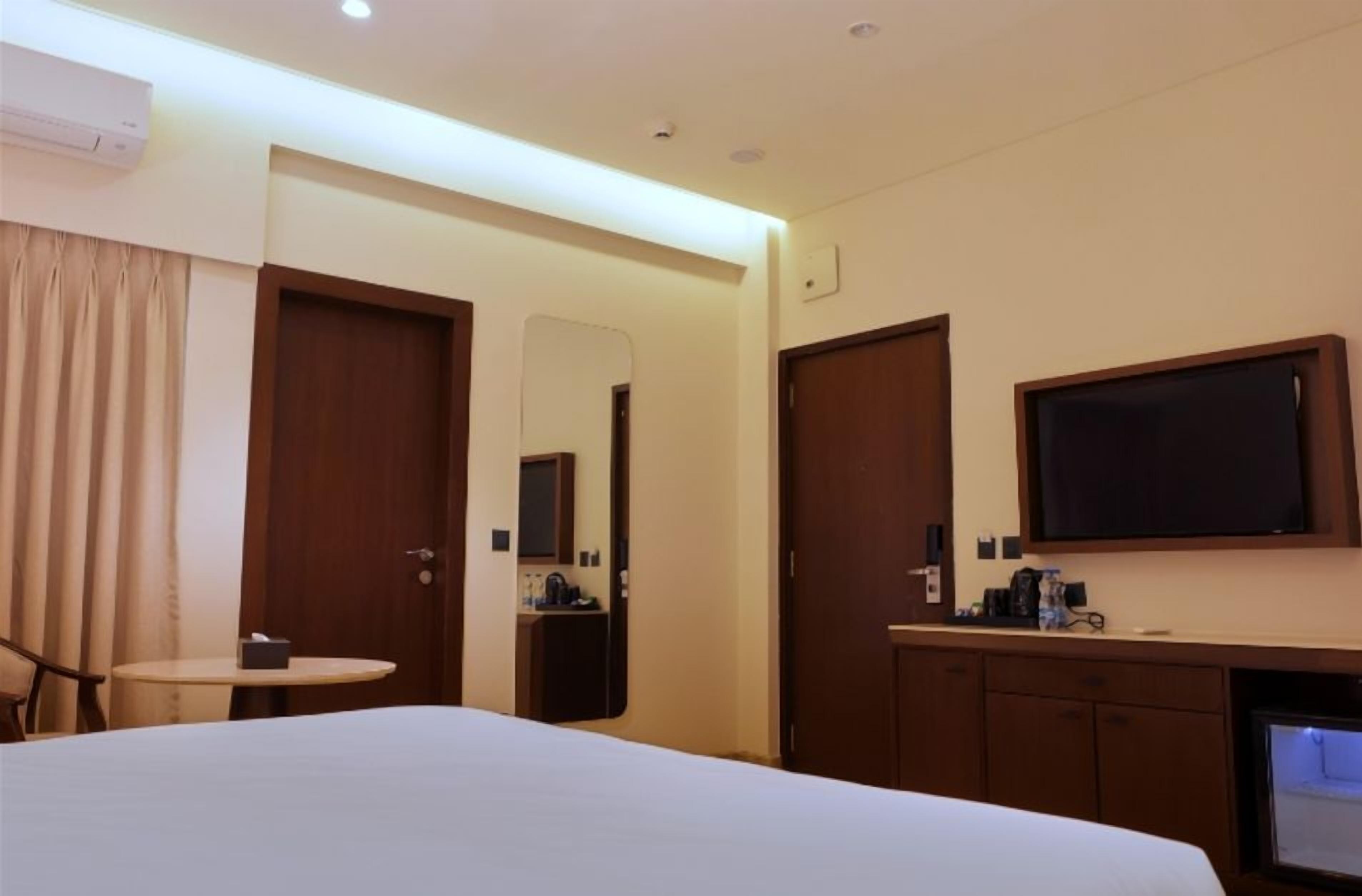 Quarto de hotel com cama, televisão na parede, mesinha e espelho.