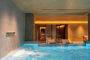 Área interna de piscina moderna com um elemento aquático, assentos e vista para um corredor.