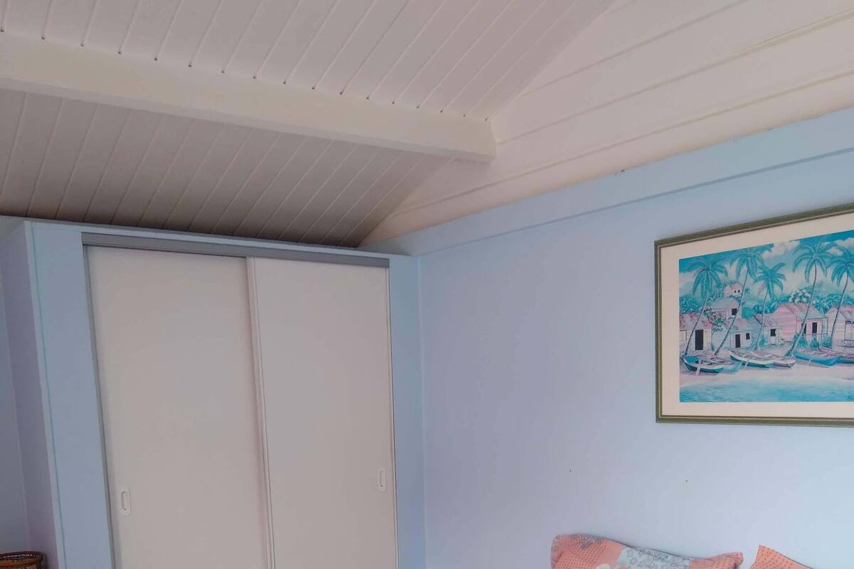 Um quarto com cama, guarda-roupa, mesa de cabeceira e um quadro na parede.