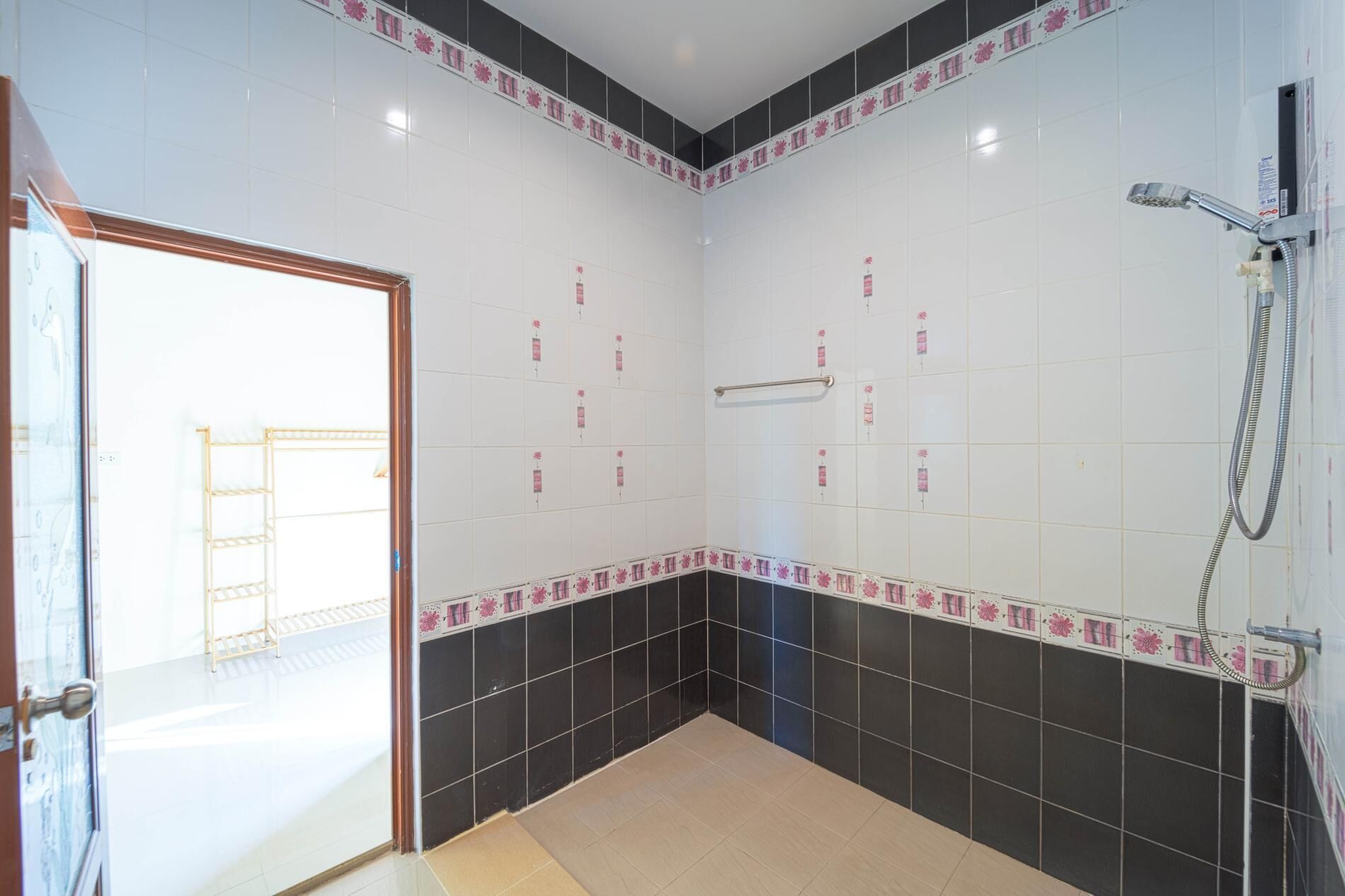 Casa de banho com azulejos brancos e negros, um chuveiro e um porta-toalhas.