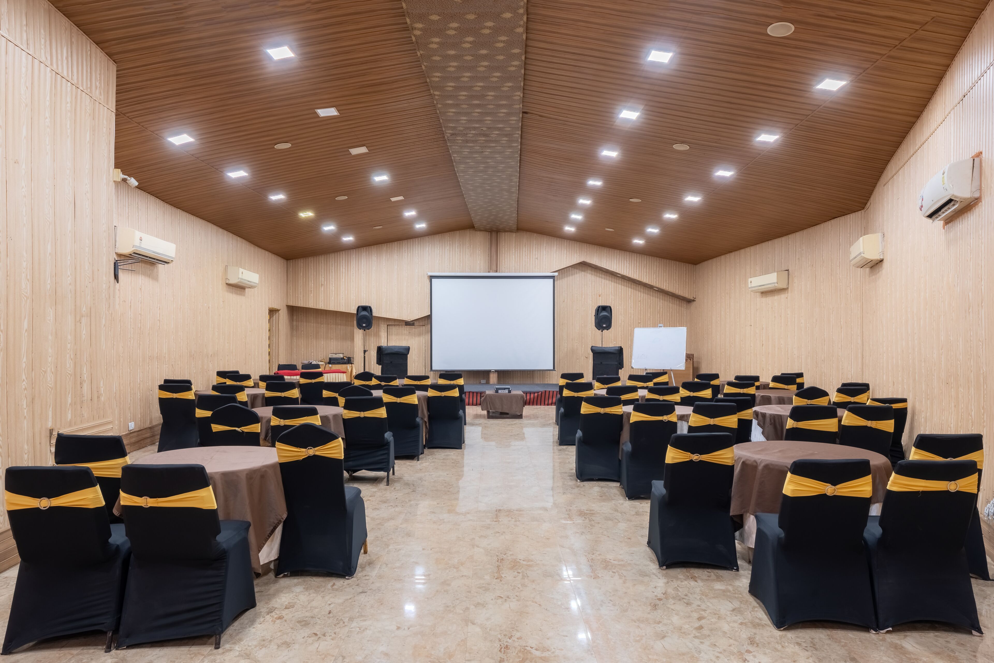 Uma sala de conferências com fileiras de cadeiras, uma tela de projeção e alto-falantes.