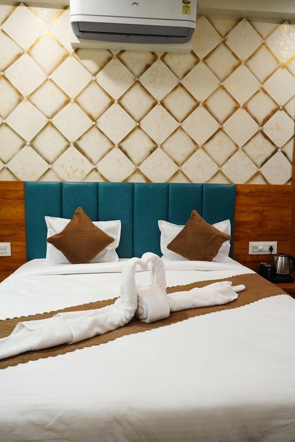 Quarto de hotel com cama, cabeceira verde-água, almofadas castanhas e brancas, cama bem arrumada com toalhas e um aparelho de ar condicionado acima da cabeceira.