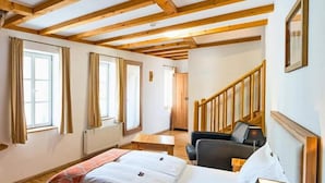 Quarto de hotel com teto de madeira, cama com edredão branco, uma cadeira, escrivaninha e luminária.