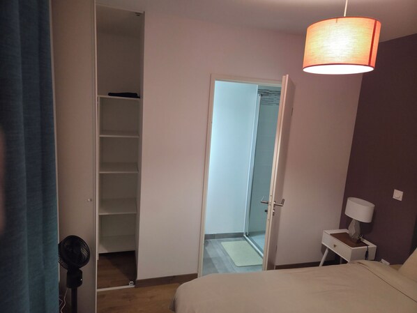 Quarto com uma cama, mesa de cabeceira com abajur, armário e porta aberta para outro cômodo.