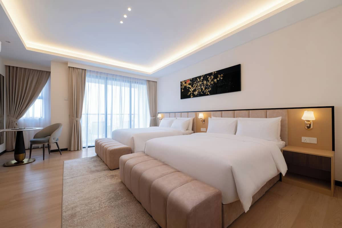 Quarto de hotel moderno com duas camas, área de estar e uma janela grande.