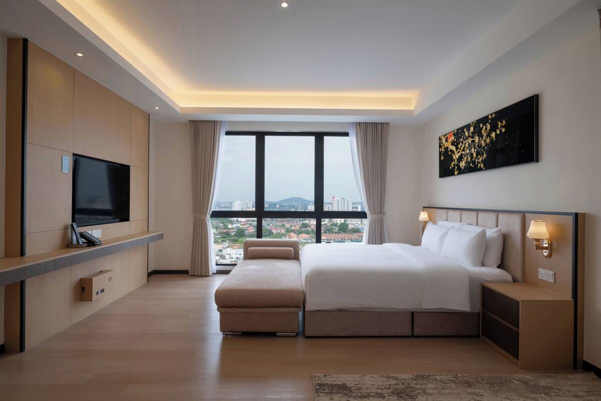 Quarto de hotel moderno com uma cama grande, televisão, escrivaninha e vista para a cidade.